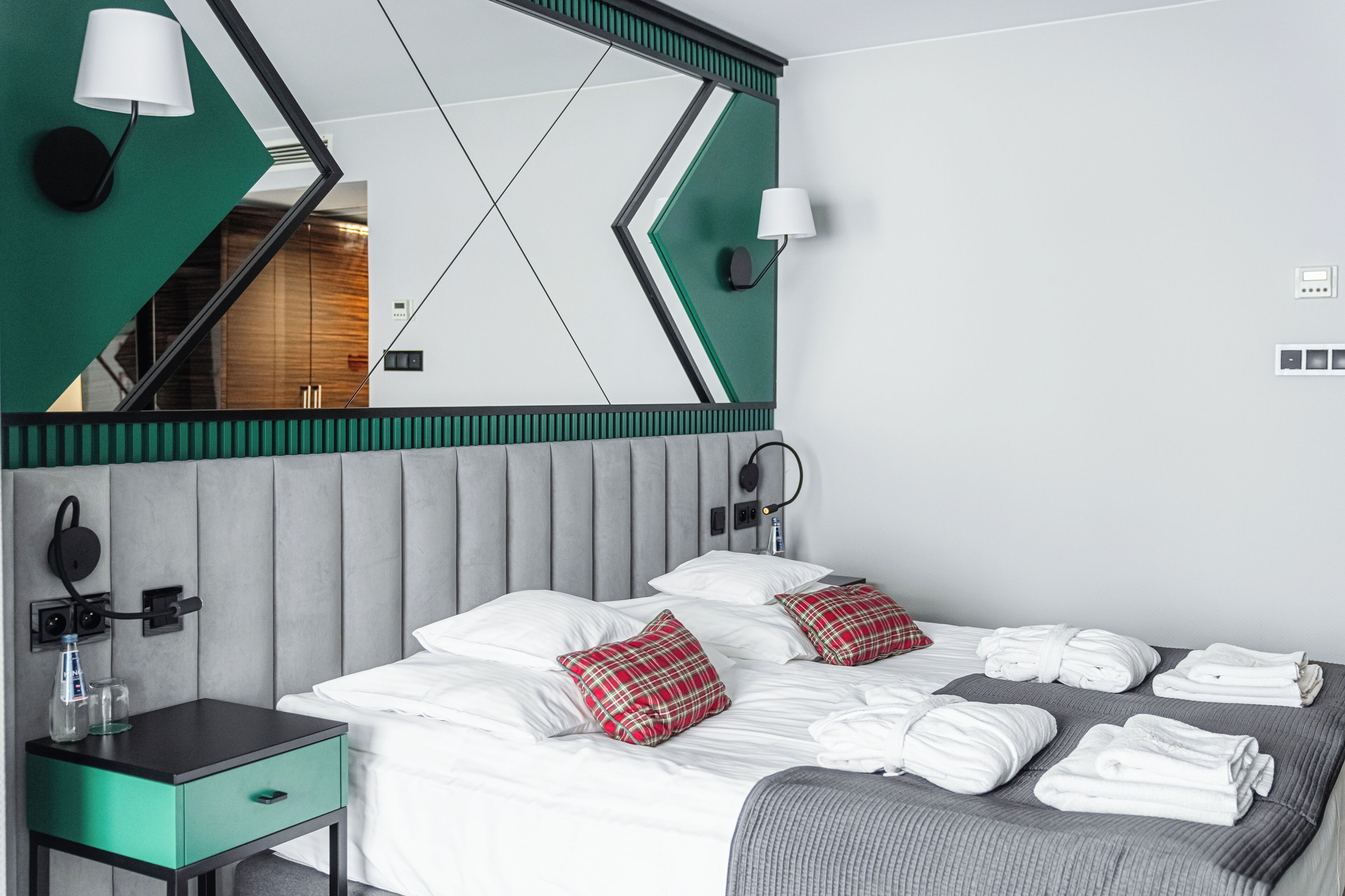 Quarto de hotel moderno com uma cama grande, uma mesinha de cabeceira, um espelho e uma parede verde.