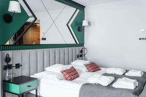 Quarto de hotel moderno com uma cama grande, uma mesinha de cabeceira, um espelho e uma parede verde.