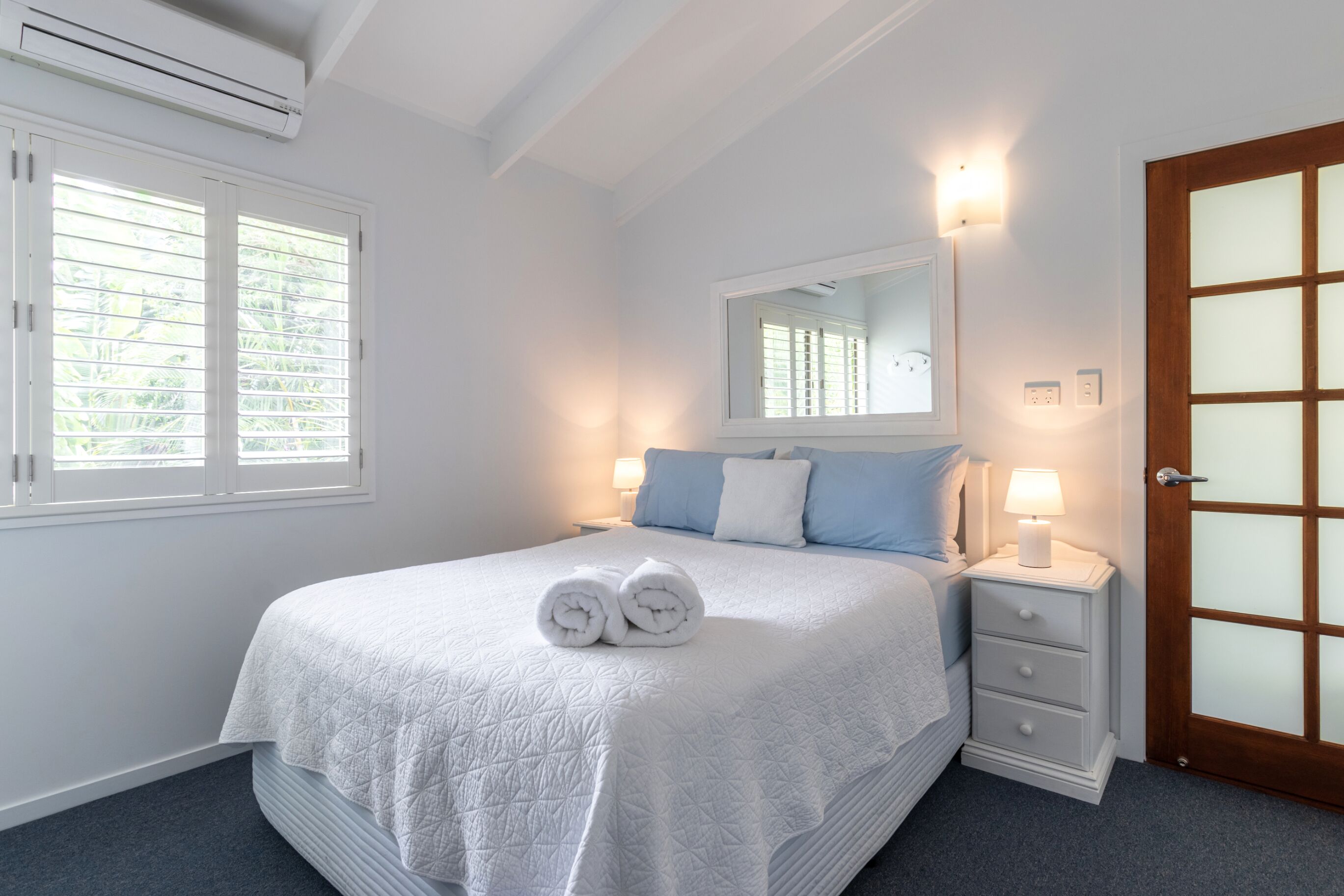 Uma cama bem arrumada com toalhas dobradas, um abajur e uma mesa de cabeceira.