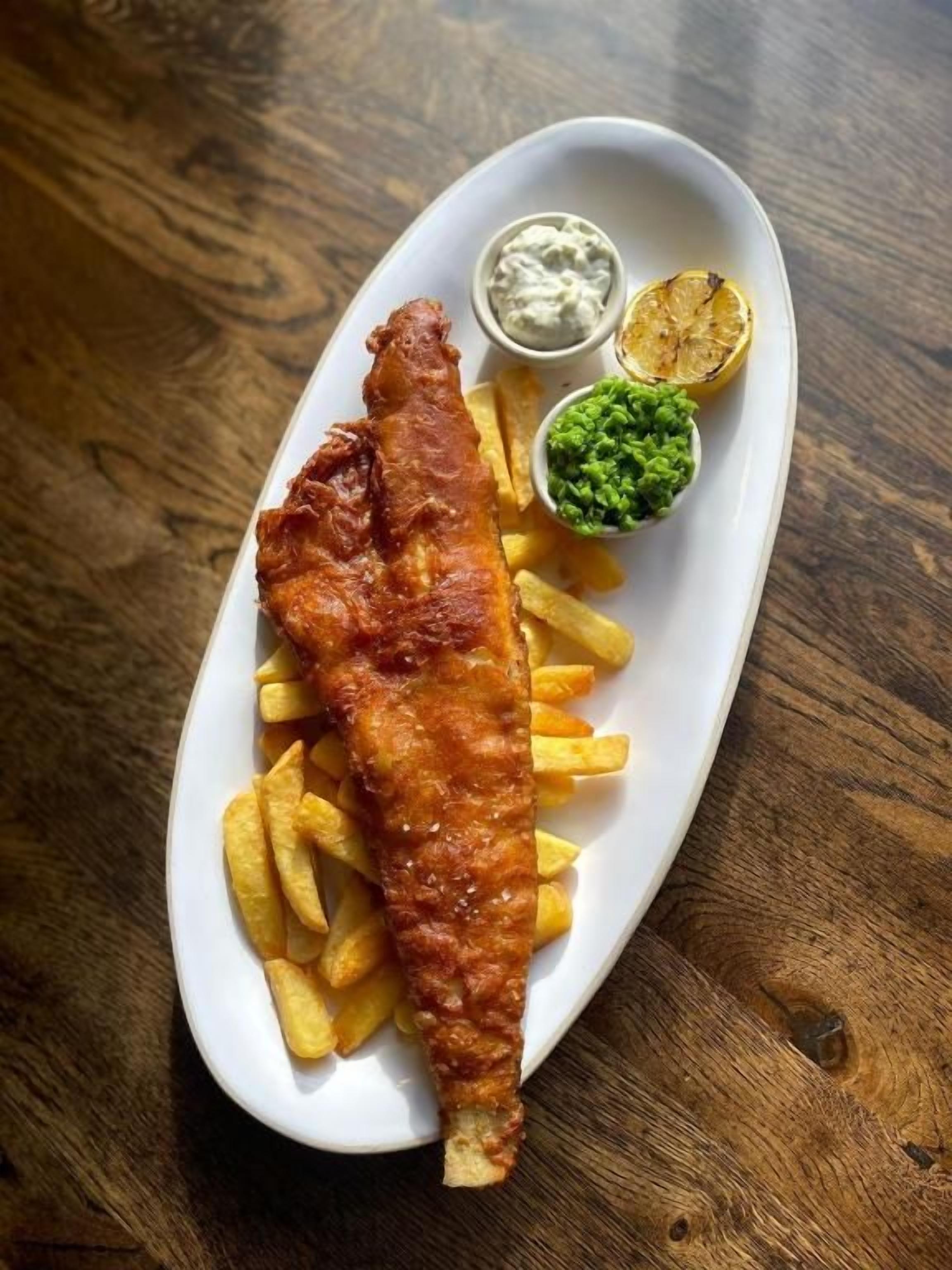 Prato com um filé de peixe grande, batatas fritas e dois pequenos recipientes de molho.