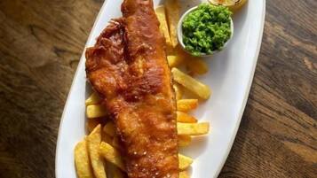 Prato com um filé de peixe grande, batatas fritas e dois pequenos recipientes de molho.