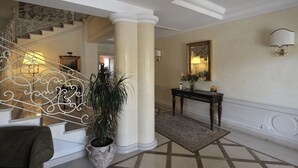 Um hall imponente com escadaria, colunas, um aparador com espelho e um vaso de planta.