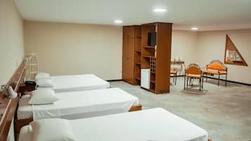 Quarto de hotel com duas camas, uma escrivaninha, uma cadeira e uma mesinha.