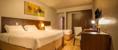 Quarto de hotel com duas camas, uma escrivaninha com luminária, televisão e um quadro na parede.