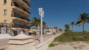 Hotel à beira-mar com várias varandas, um calçadão de areia e palmeiras.