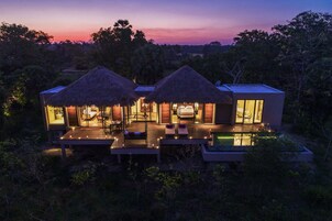 Uma villa moderna com duas construções de telhado de palha, piscina e área de deck.
