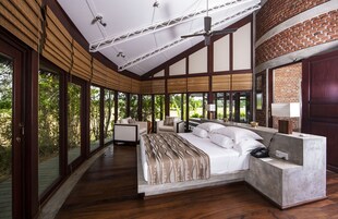 Quarto espaçoso com uma cama grande, uma escrivaninha e vista para o verde através de amplas janelas.