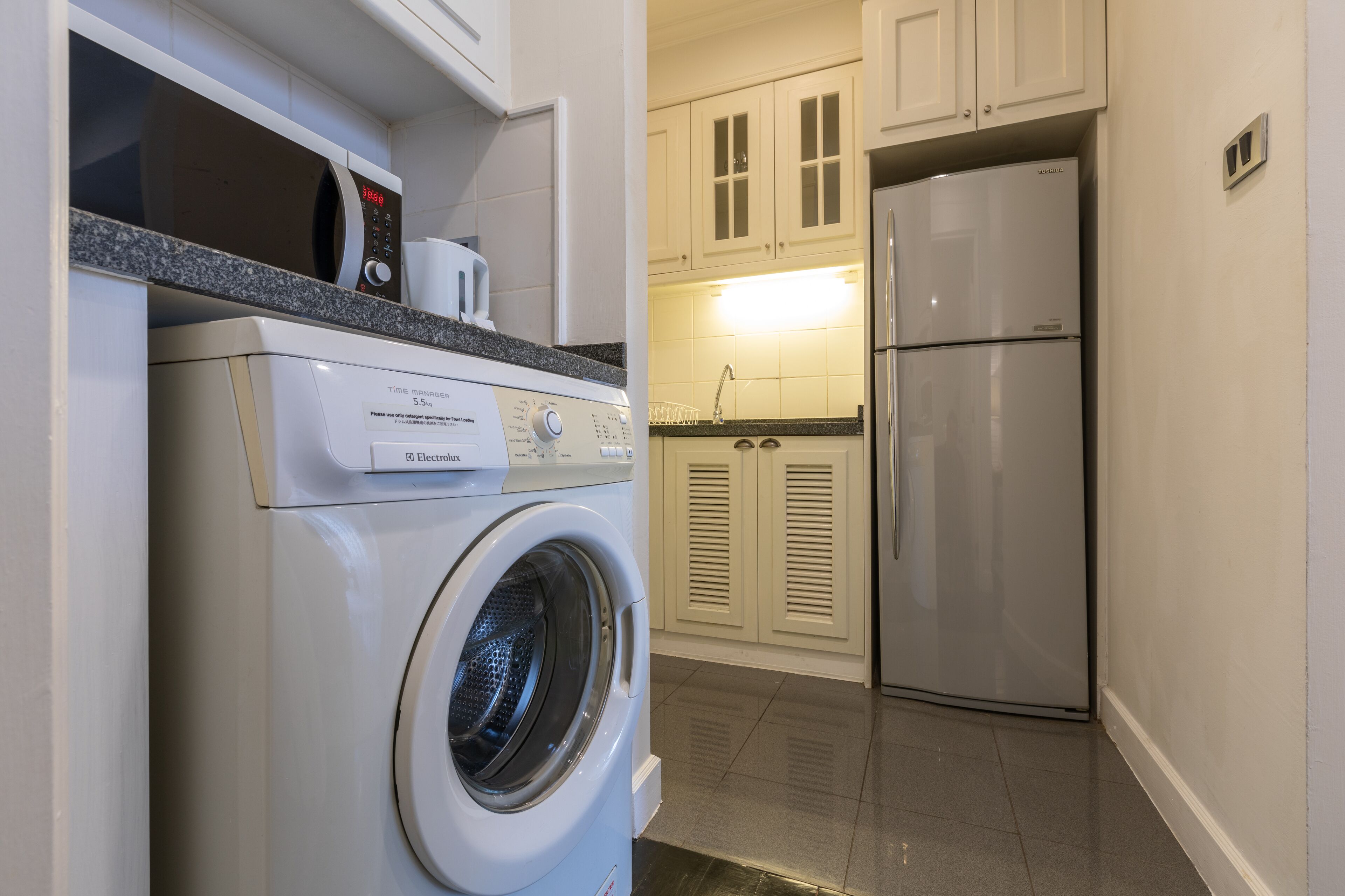Cozinha compacta com máquina de lavar, micro-ondas e frigorífico.
