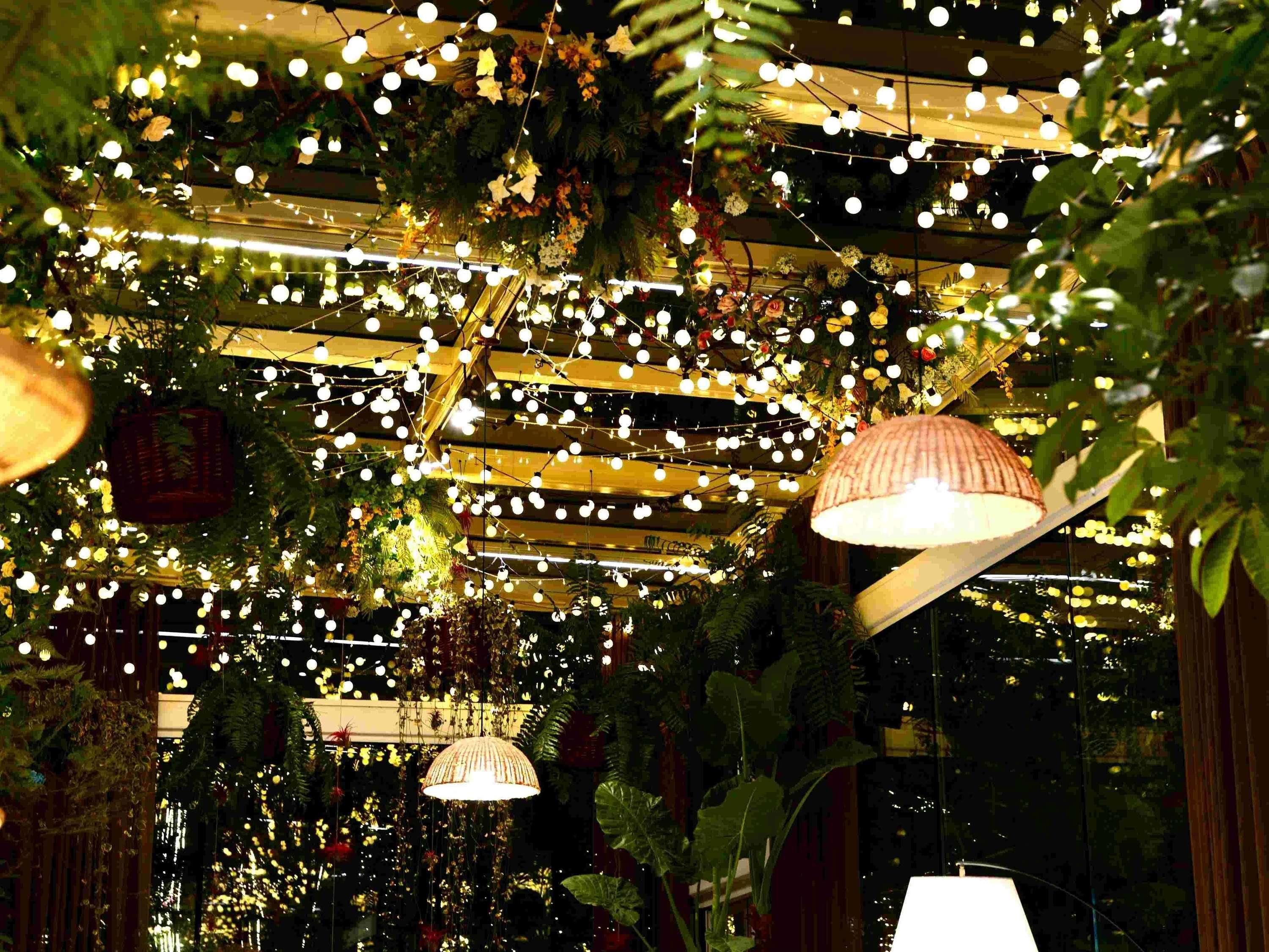 Espaço interno com luminárias pendentes, plantas e estrutura no teto.