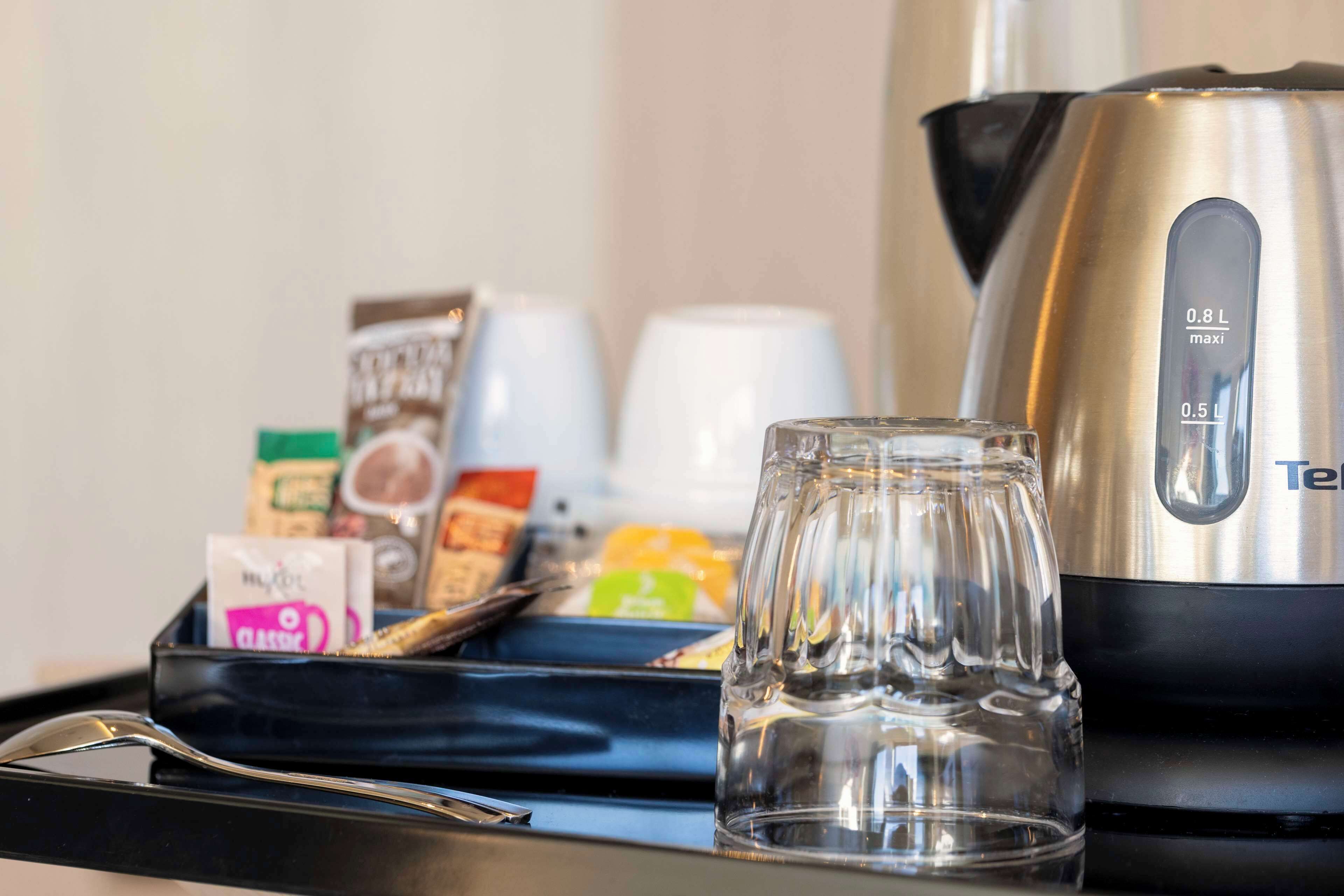 Uma cafeteira, um copo e vários sachês de café sobre uma bandeja.