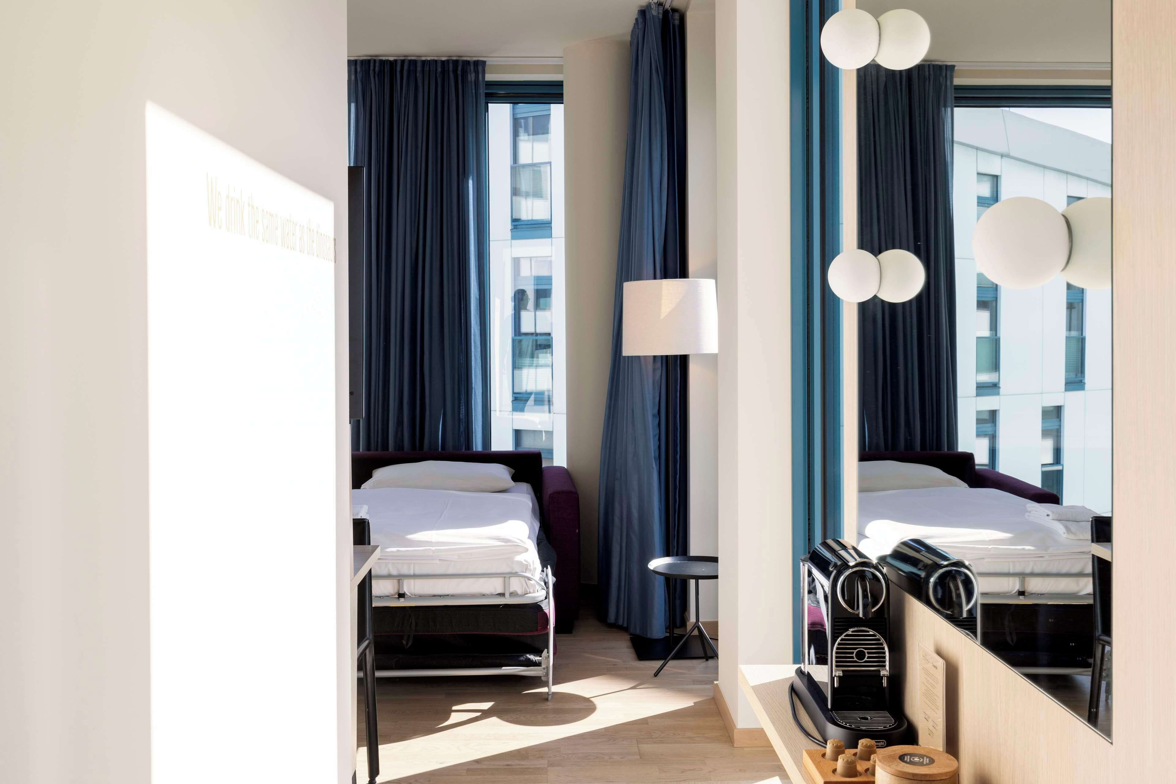 Quarto de hotel com duas camas, uma escrivaninha, máquina de café e uma janela grande com cortinas.