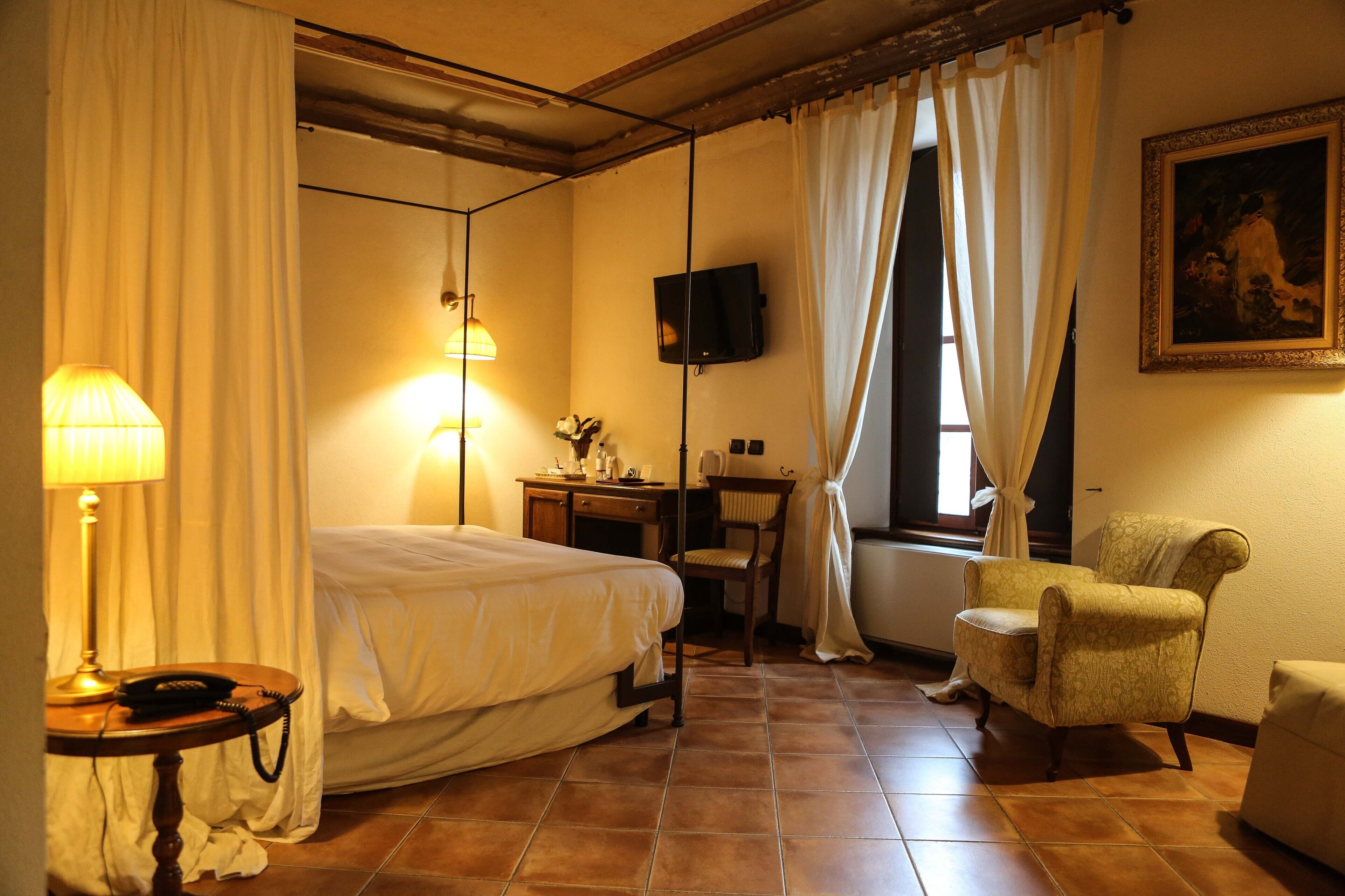 Quarto de hotel com cama, escrivaninha, cadeira, televisão e um quadro na parede.