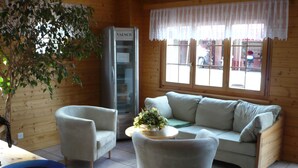 Um quarto acolhedor com decoração em madeira, um sofá, duas poltronas, uma mesinha de centro com um vaso, e uma geladeira Valser.