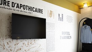 Parede com televisão de tela plana, porta-toalhas fixado na parede e uma cama com mala.