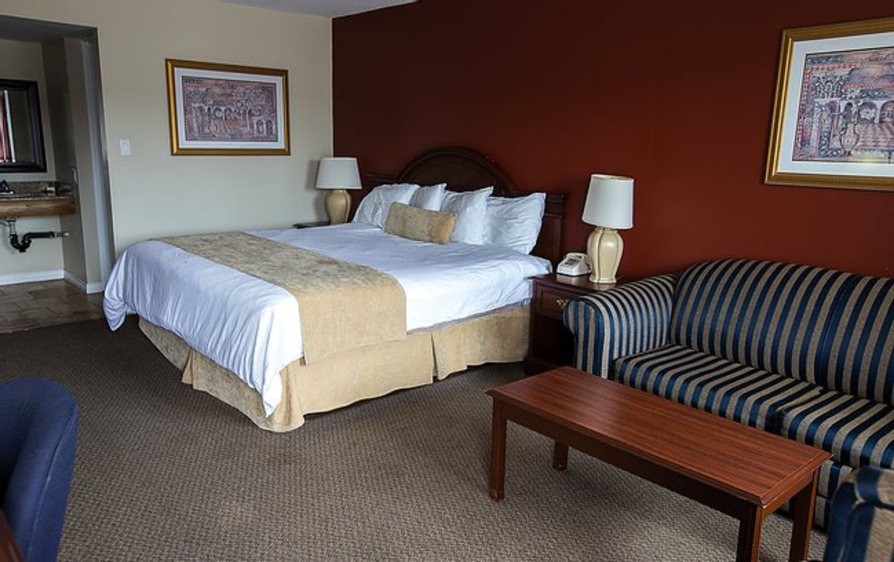 Quarto de hotel com uma cama grande, um sofá, uma mesa pequena e duas luminárias.