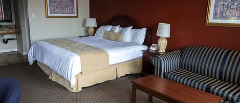 Quarto de hotel com uma cama grande, um sofá, uma mesa pequena e duas luminárias.