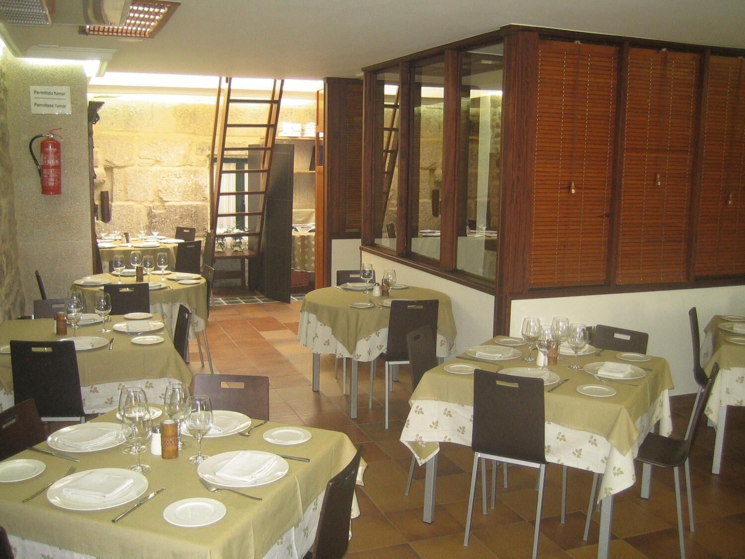 Uma sala de jantar com mesas preparadas para refeições, um extintor de incêndio e uma escada encostada à parede.