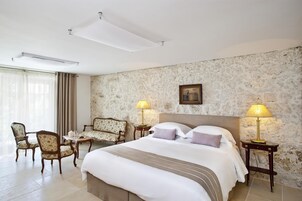 Quarto de hotel com uma cama grande, duas mesas de cabeceira com luminárias, uma cadeira, uma mesa pequena e um sofá.