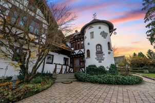 Um edifício tradicional em estilo europeu com uma torre, uma escadaria de madeira e um caminho de tijolos que leva à entrada.