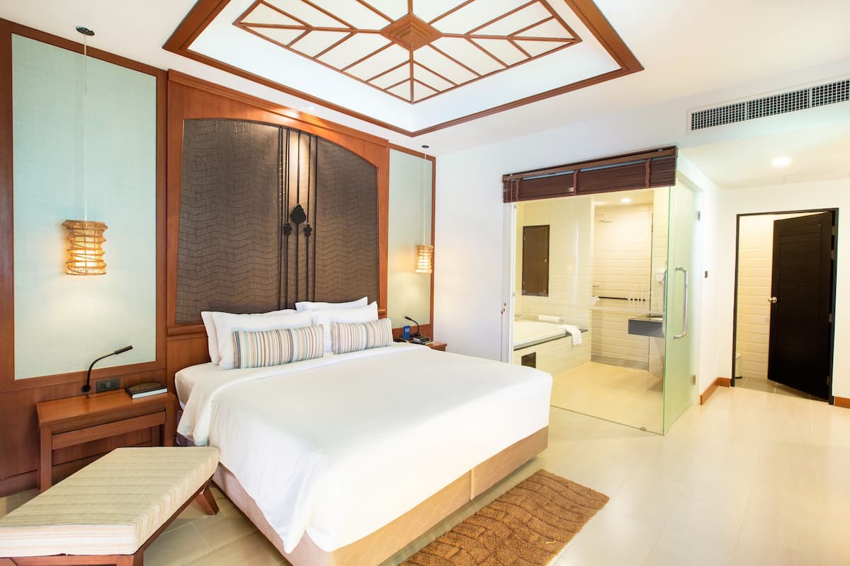 Quarto de hotel moderno com uma cama grande, mesas de cabeceira, uma escrivaninha e área de chuveiro com divisória de vidro.
