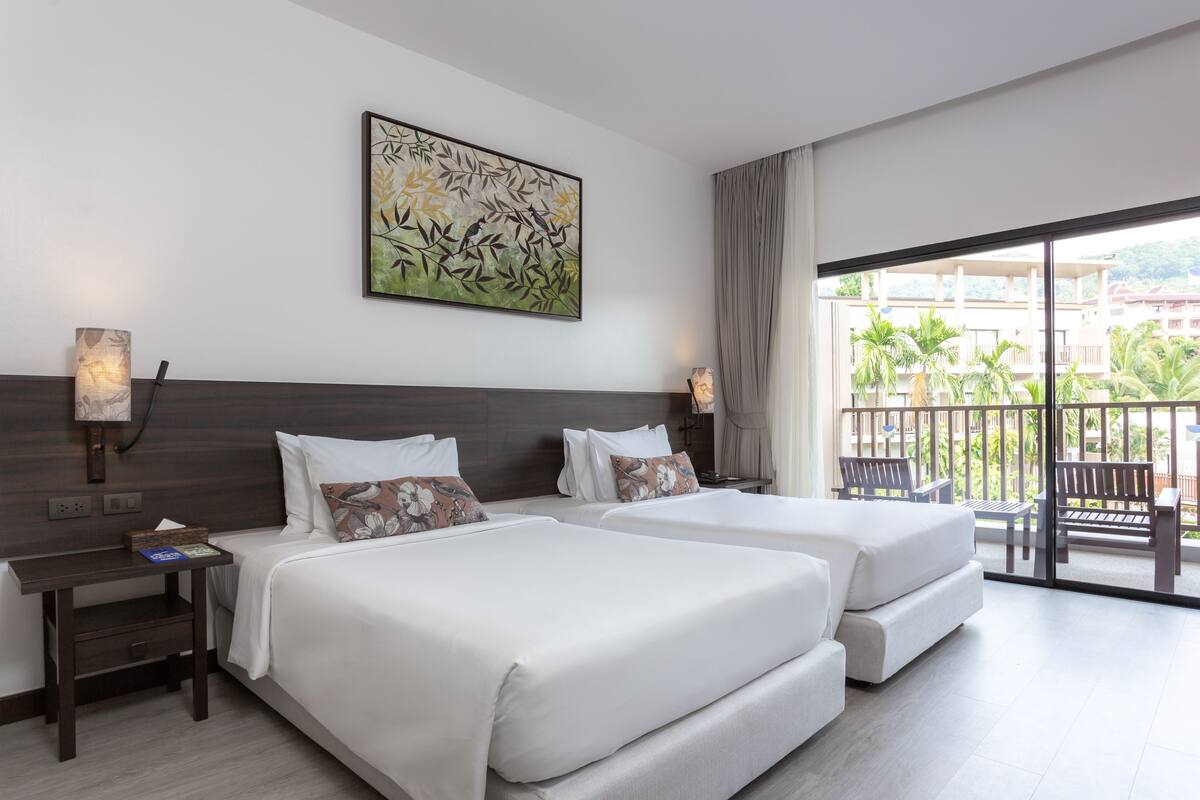 Quarto de hotel com duas camas, uma mesa de cabeceira, uma obra de arte pendurada na parede e varanda com área de estar externa.