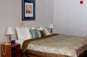 Uma cama bem arrumada com colcha estampada, duas luminárias de cabeceira, uma mesa de cabeceira com telefone e um quadro na parede.