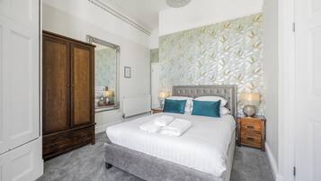 Quarto com cama grande, guarda-roupa, espelho e papel de parede estampado.