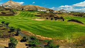 Um campo de golfe com bunkers, green de putting e um clube em segundo plano.