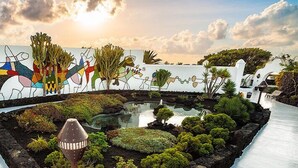 Um jardim com lago, bancos e um mural na parede.