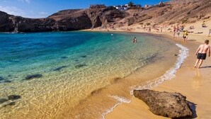 Uma praia com águas turquesa cristalinas, areal arenoso e afloramentos rochosos.