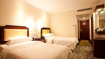 Quarto de hotel com duas camas, mesa de cabeceira, escrivaninha com abajur, espelho e porta que dá para um corredor.