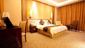 Quarto de hotel com uma cama grande, uma escrivaninha com um laptop, uma cadeira, uma mesa de cabeceira e um abajur.