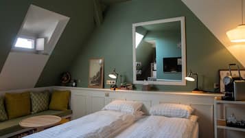 Um quarto acolhedor com teto inclinado, um banco embutido com almofadas, uma cama com colcha xadrez, uma mesa de cabeceira e um espelho sobre a cama.