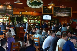 Um bar cheio, com móveis de madeira e diversas garrafas nas prateleiras.