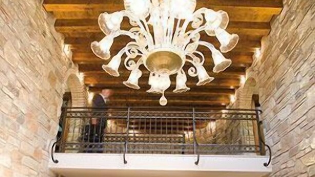 Um salão imponente com um candelabro, uma escadaria e uma mesa com arranjo floral.