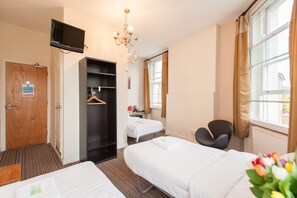 Quarto de hotel com duas camas, televisão presa na parede, guarda-roupa, secretária com candeeiro e uma cadeira.