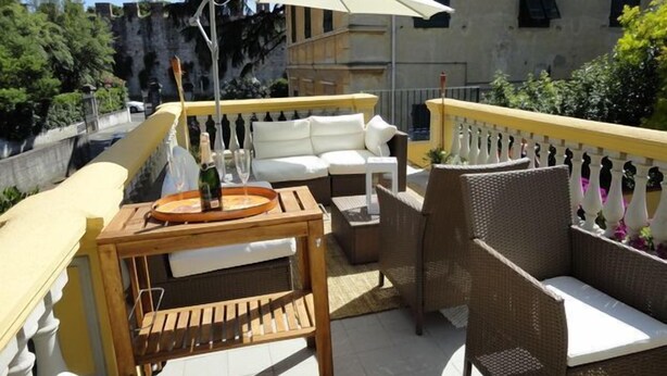 Um pátio externo com mesa de madeira, cadeiras de vime, sofá branco e guarda-sol.