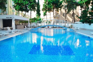 Uma piscina com uma ponte, espreguiçadeiras e um bar na piscina.