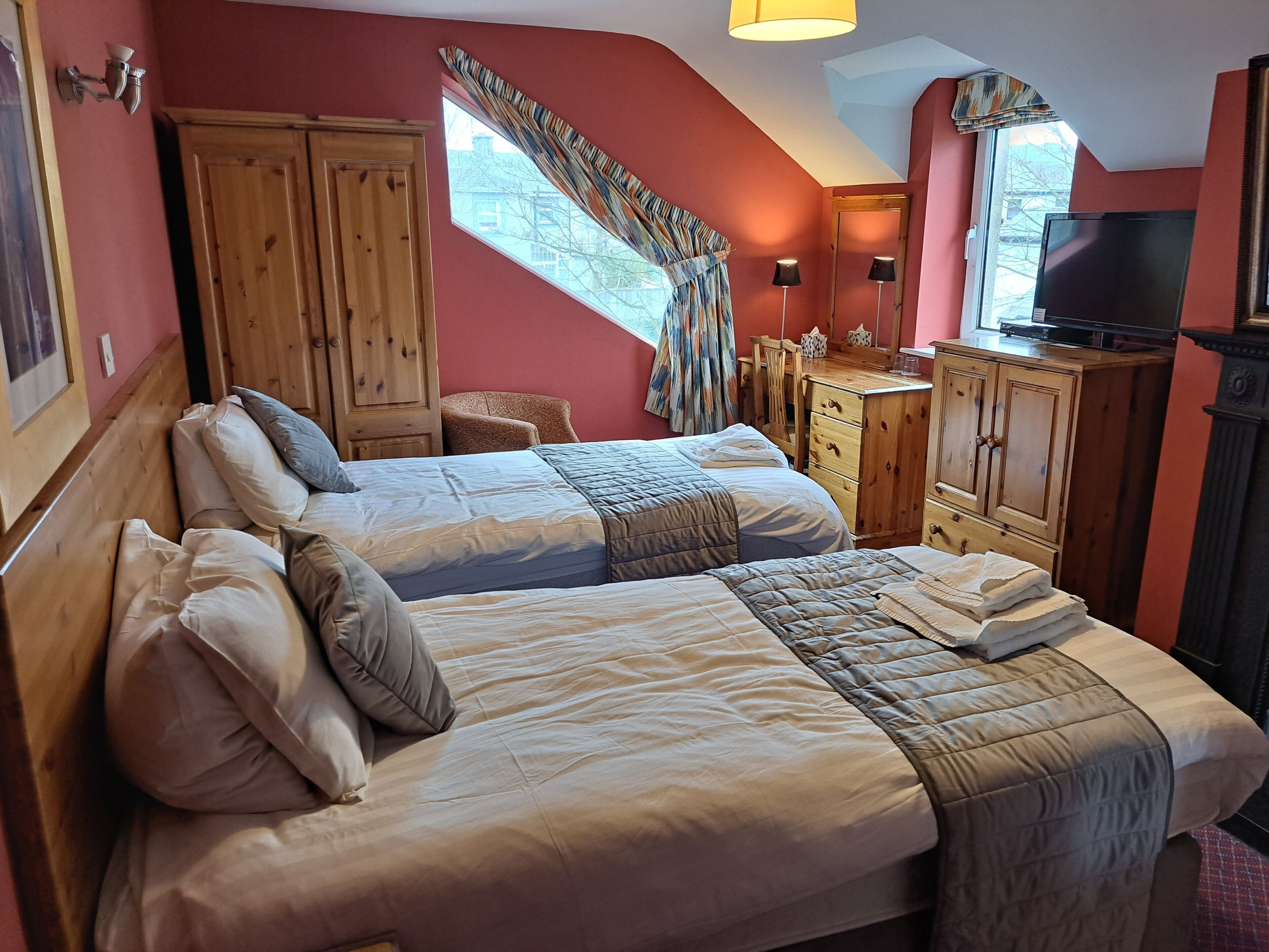 Quarto com duas camas, móveis de madeira, uma televisão e uma janela com cortinas.