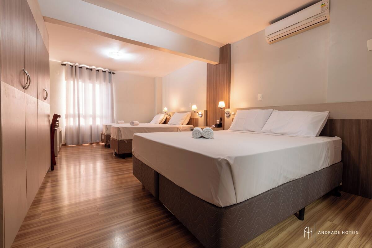 Quarto de hotel com uma cama grande, uma cama menor, uma escrivaninha e um banheiro.