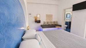 Quarto moderno com cama, mesa de cabeceira e um pequeno espaço de estar com almofadas.