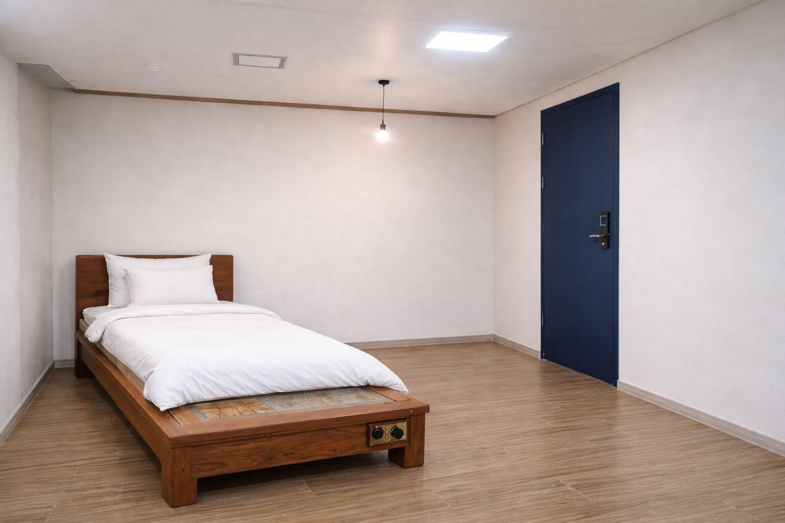 Quarto com cama de madeira, roupa de cama branca, porta azul e luminária no teto.