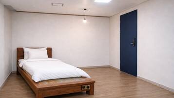 Quarto com cama de madeira, roupa de cama branca, porta azul e luminária no teto.