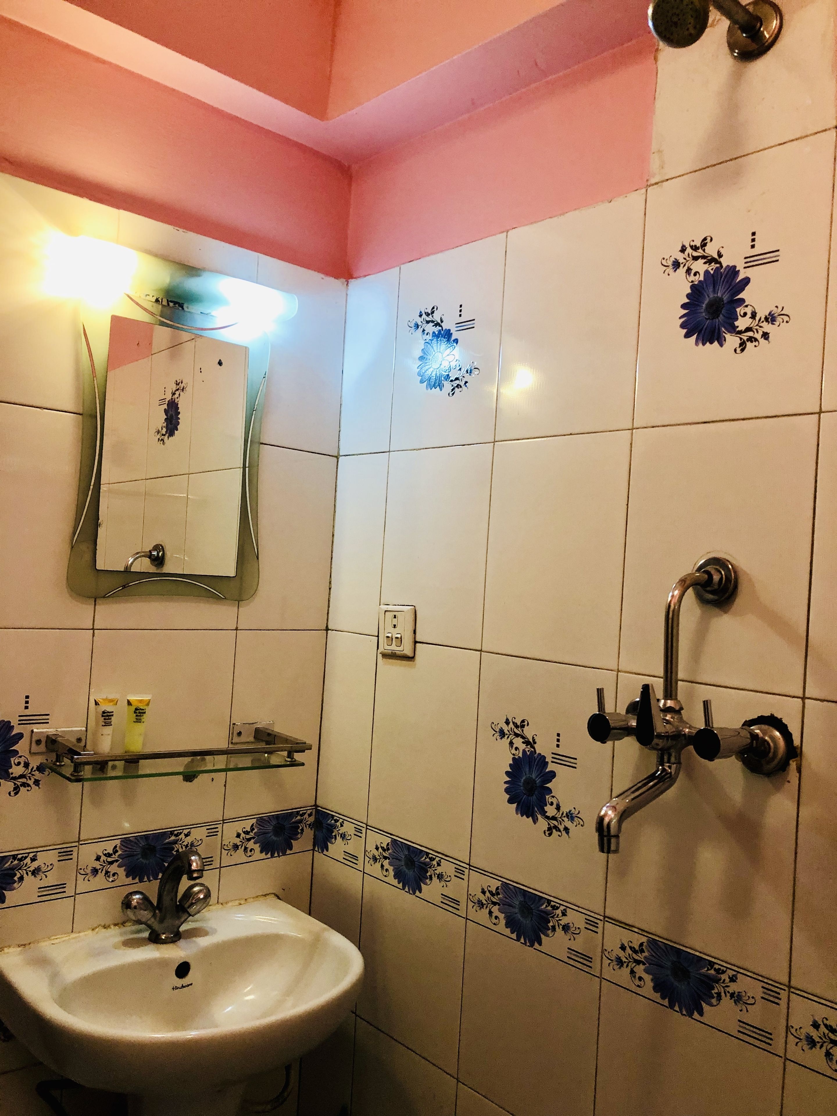 Casa de banho com lavatório branco, espelho e chuveiro.