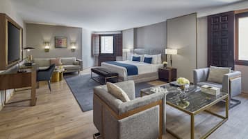 Quarto de hotel com cama, duas poltronas, um sofá, uma escrivaninha e uma mesa de centro.
