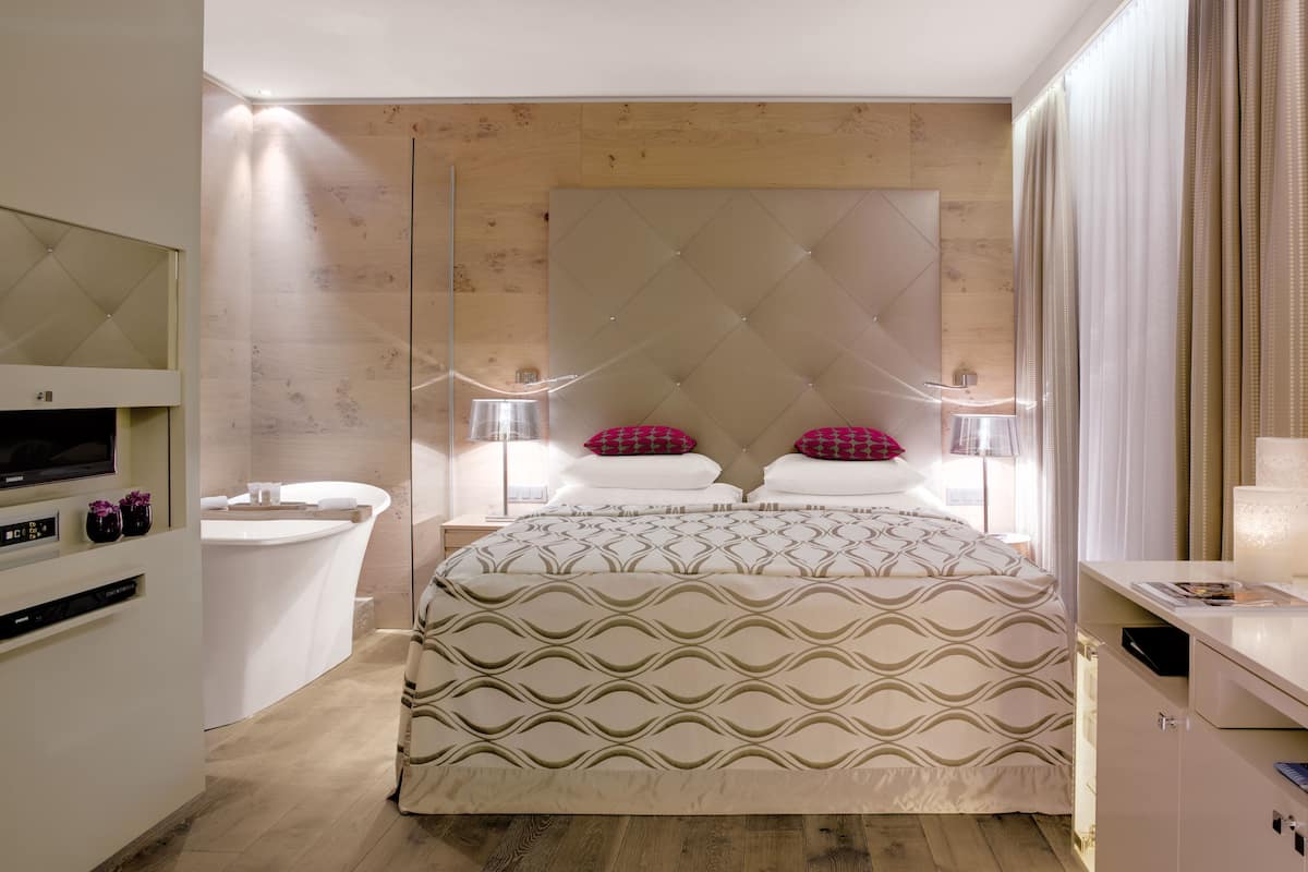 Quarto moderno com uma cama grande, abajures, televisão e banheiro com banheira.