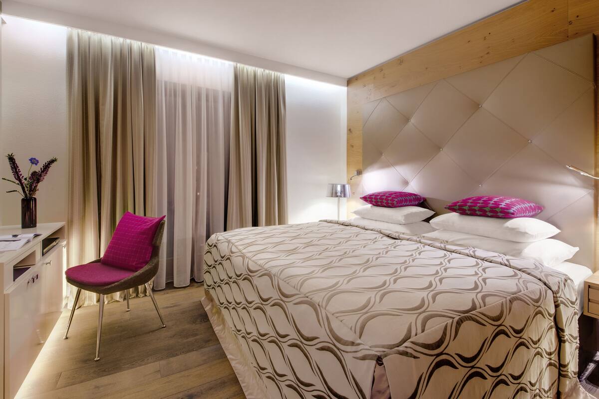 Quarto de hotel moderno com uma cama grande, uma escrivaninha com um computador, uma cadeira e uma janela com cortinas.