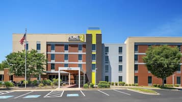 Um hotel moderno com um letreiro chamativo 'HOME 2', entrada coberta e estacionamento com vagas para deficientes.