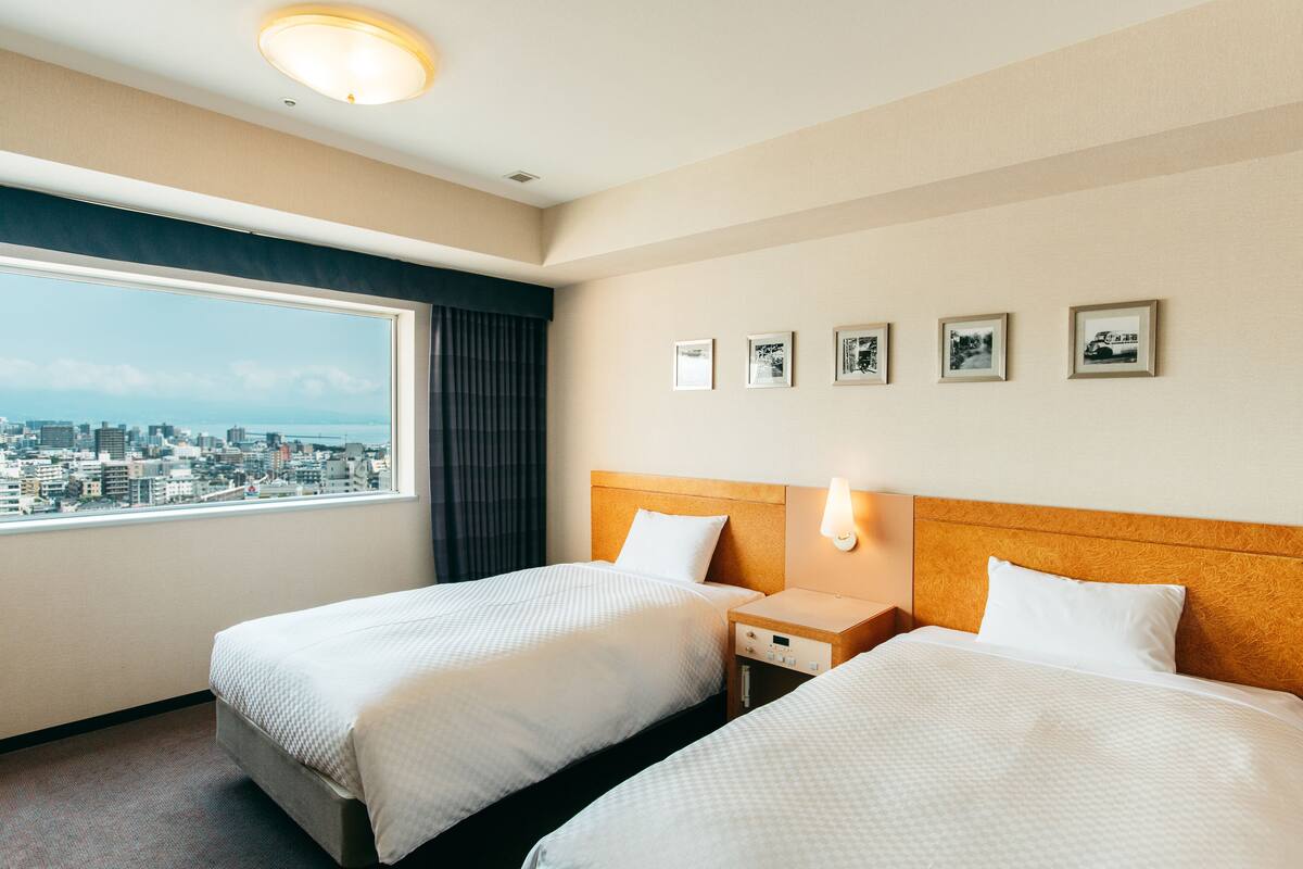 Quarto de hotel com duas camas, vista para a cidade e parede com quadros.