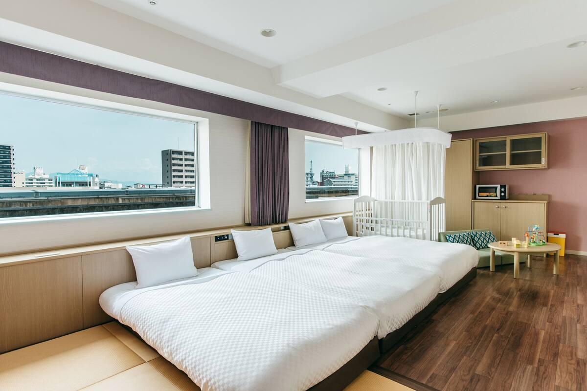 Quarto de hotel moderno com cama grande, vista para a cidade e um pequeno espaço de estar.